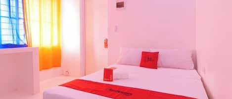 Quarto de hotel com cama, manta vermelha e janela com cortinas.
