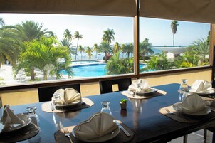 Mesa de jantar posta para quatro com vista para uma piscina e palmeiras.
