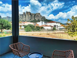 Uma varanda com cadeiras de vime, uma mesa pequena e vista para edifícios e montanhas rochosas.
