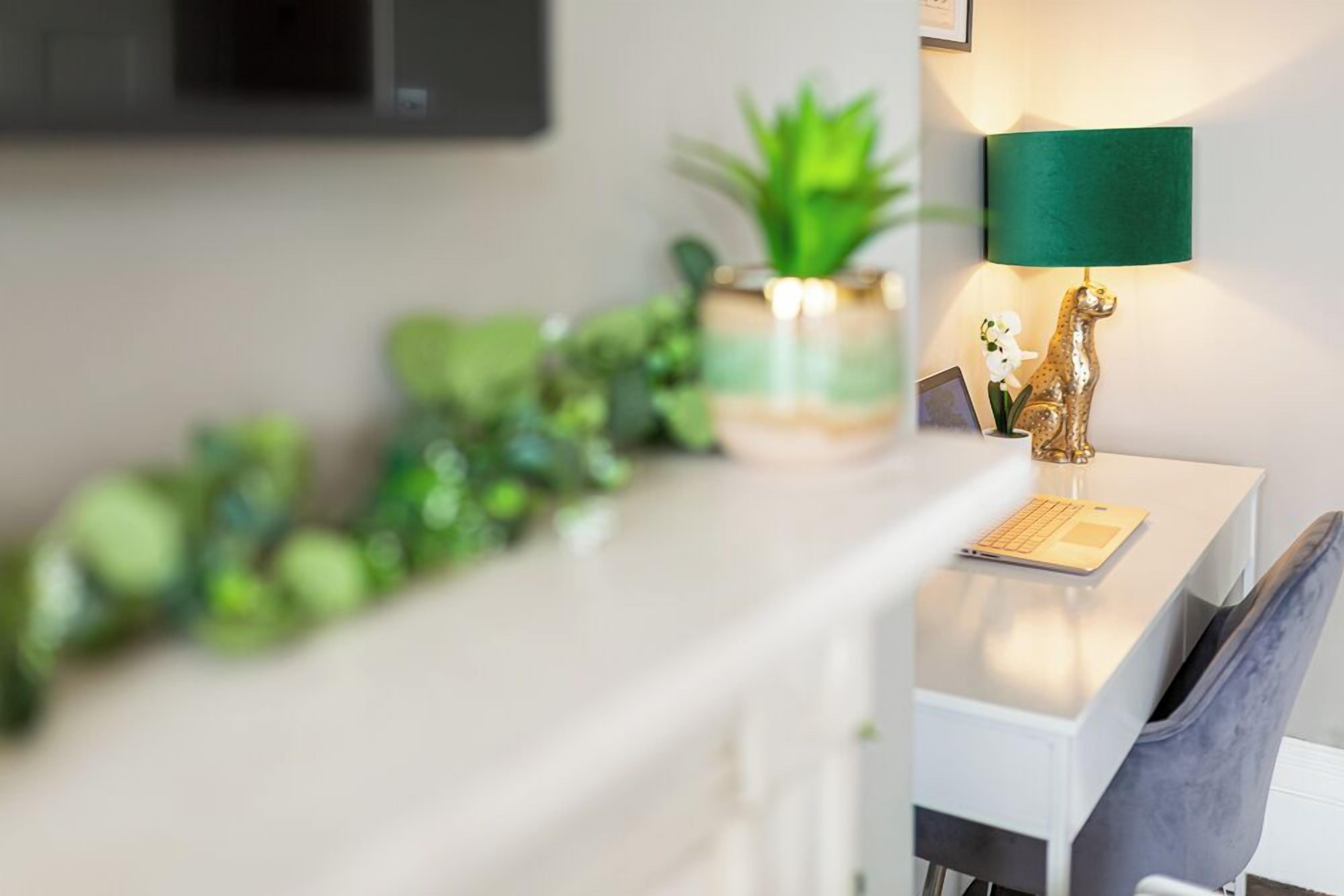 Uma cozinha moderna com bancada branca, uma planta verde, um abajur decorativo e um laptop.