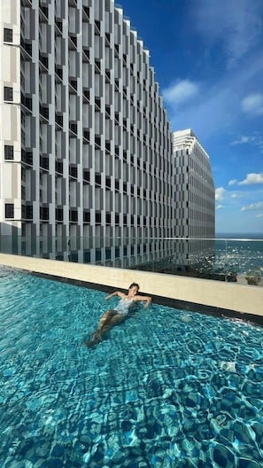 Uma pessoa nadando em uma piscina com um edifício moderno ao fundo.