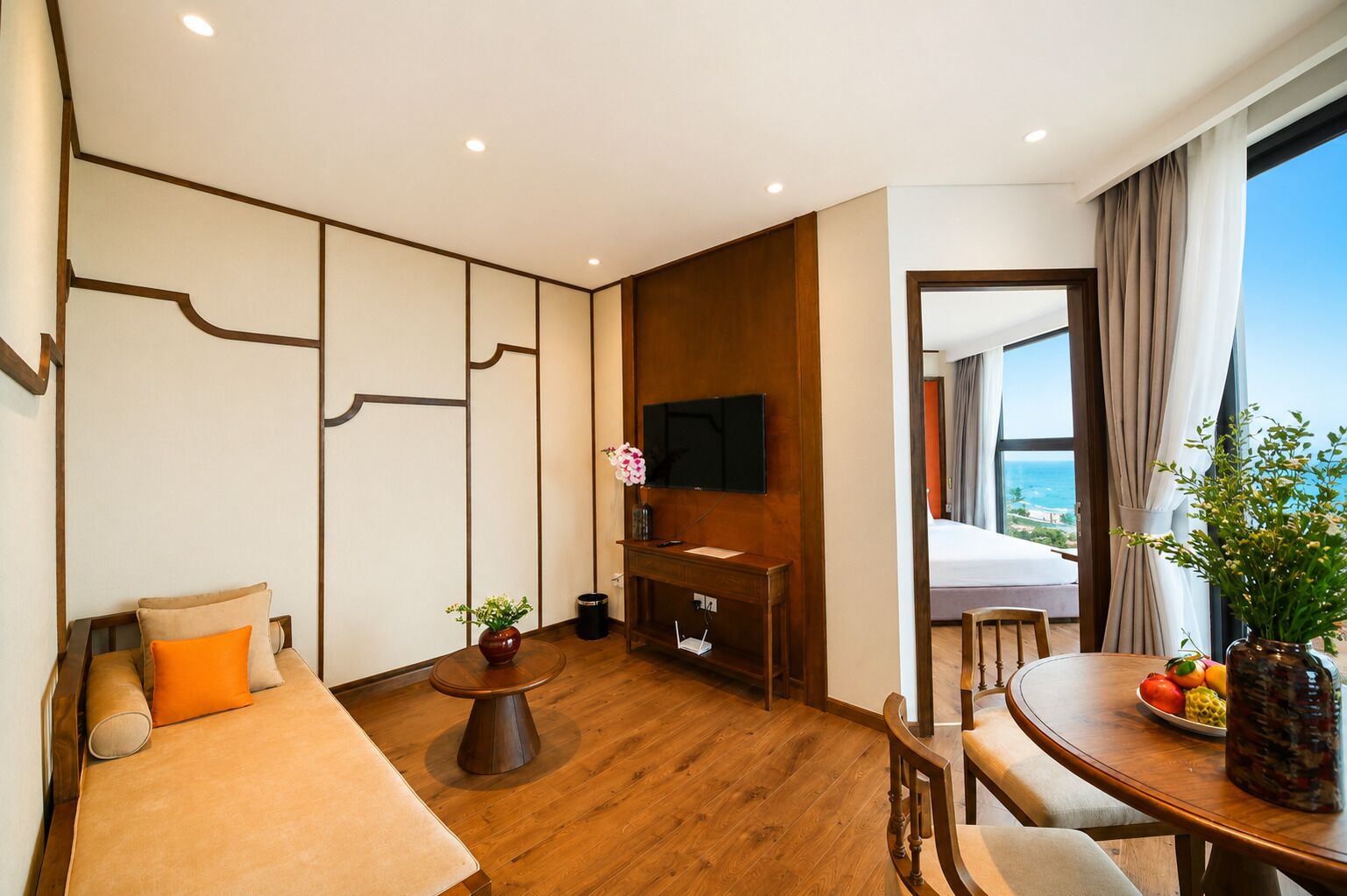 Quarto de hotel com sofá, mesa de jantar, televisão e vista para o oceano.