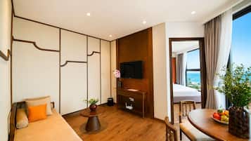 Quarto de hotel com sofá, mesa de jantar, televisão e vista para o oceano.