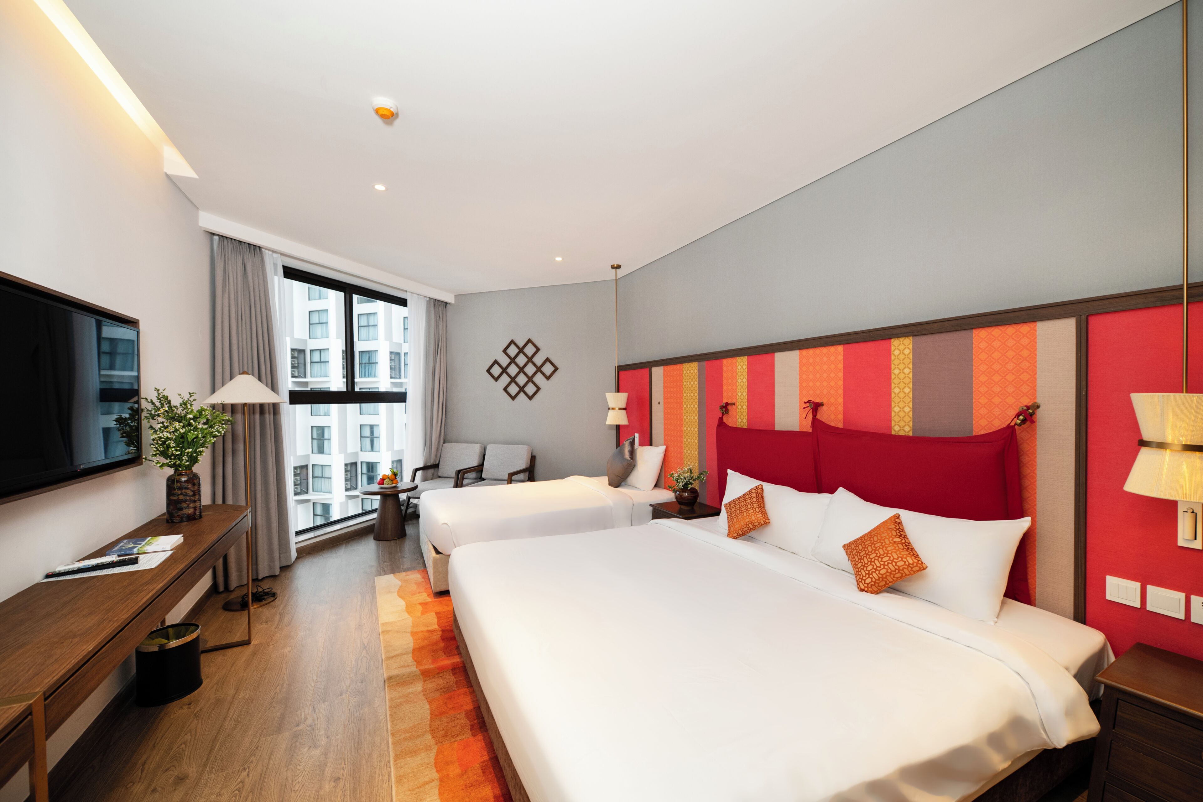 Quarto de hotel com duas camas, televisão, escrivaninha e janela com vista para edifícios.