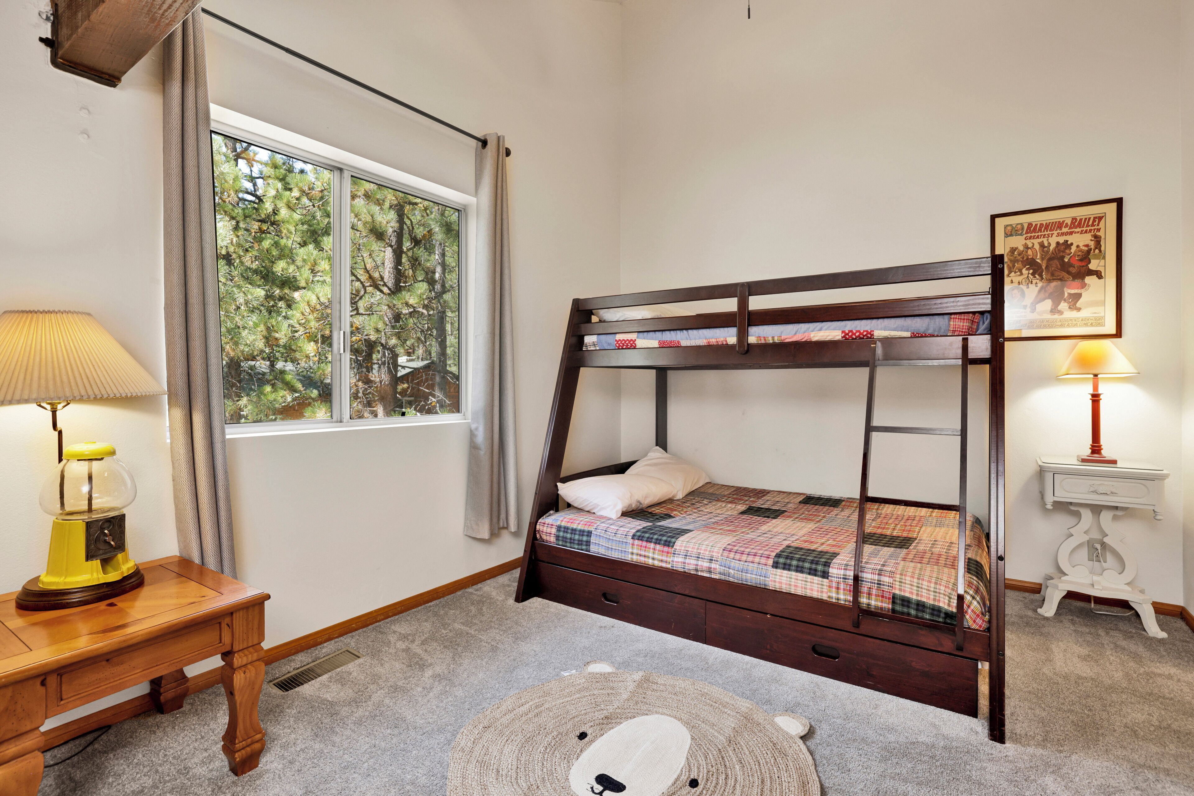 Quarto com uma cama de solteiro, mesa de cabeceira com luminária, janela com cortinas e um pôster na parede.