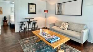 Uma sala de estar com uma mesa de centro de madeira, um sofá cinza, um tapete estampado e um ventilador de teto.