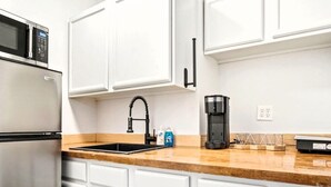 Uma cozinha moderna com armários brancos, uma geladeira de aço inoxidável, uma cafeteira preta e uma pia com torneira preta.