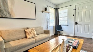 Uma sala de estar com sofá, mesa de centro e uma porta com puxador.