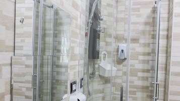 Casa de banho moderna com chuveiro em cabine de vidro, lavatório branco com espelho e azulejos bege estampados.