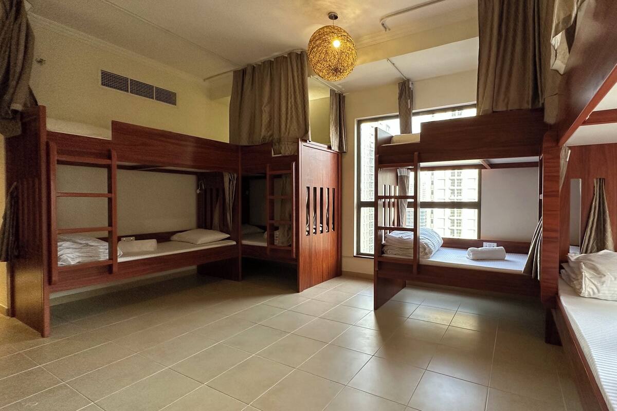 Quarto tipo dormitório com beliches, um guarda-roupa e uma luminária suspensa.