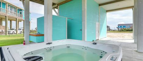 Uma área de hidromassagem com um deck coberto, vista para um edifício com revestimento azul-turquesa e uma área gramada ao fundo.