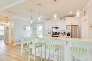 Cozinha moderna com armários brancos, uma ilha central com banquetas, eletrodomésticos de aço inoxidável e iluminação pendente.