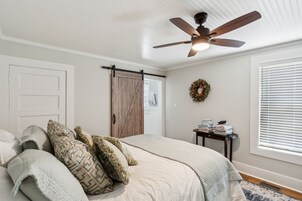 Quarto com cama, almofadas, ventoinha no teto, guarda-roupa, mesa pequena com toalhas e janela com persianas.