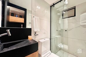 Casa de banho moderna com bancada preta, cabine de chuveiro em vidro e sanita branca.