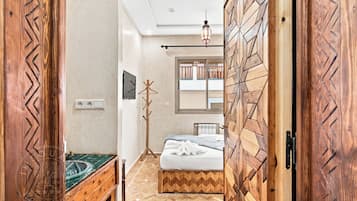 Quarto com piso em padrão herringbone, cama com roupa de cama branca, porta-roupas de madeira e luminária no teto.