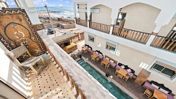 Um deque externo em vários níveis com piscina, áreas de estar e vista para a praia.