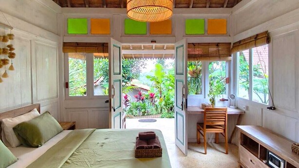 Quarto com cama, escrivaninha e vista para o verde lá fora.