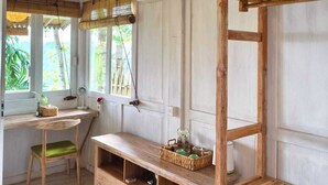 Quarto com teto de madeira, uma cama beliche, uma mesa pequena com cadeira, janela com persianas e unidade de ar condicionado.