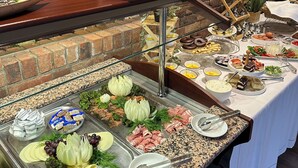 Buffet com diversos alimentos e parede de tijolos ao fundo.