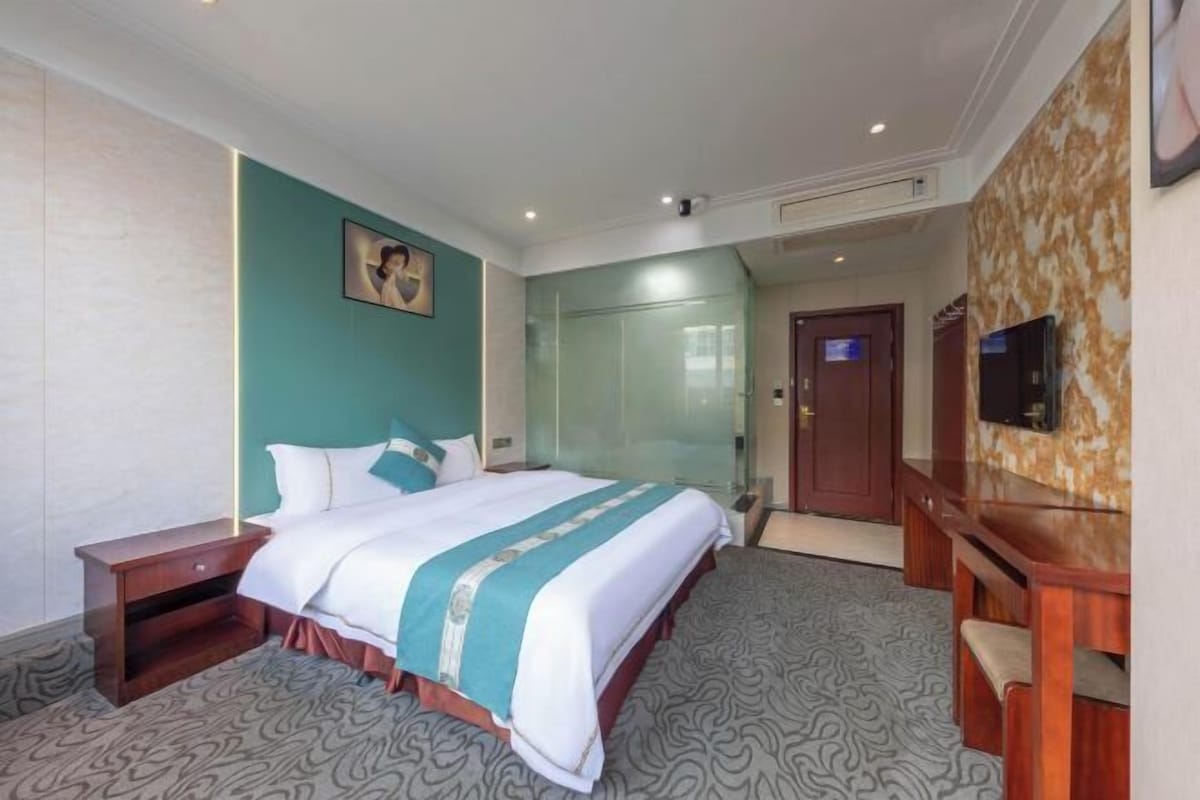 Quarto de hotel com uma cama grande, televisão presa à parede e porta de vidro que dá para o banheiro.