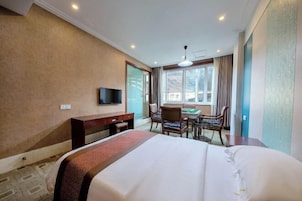 Quarto de hotel com uma cama grande, uma escrivaninha com cadeira, televisão e janela com cortinas.
