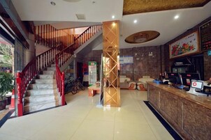 Um saguão de hotel com escada, balcão de recepção e um grande pilar.