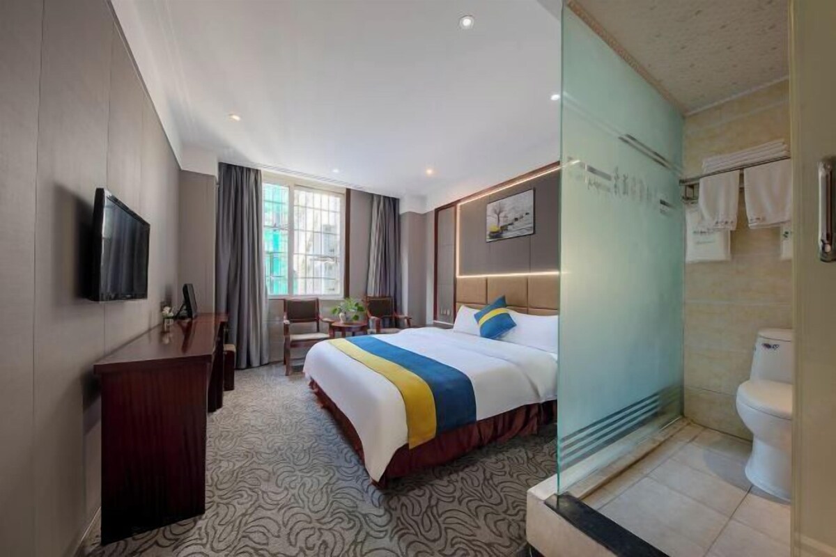 Quarto de hotel com cama, escrivaninha, televisão e banheiro.