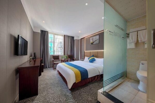Quarto de hotel com cama, escrivaninha, televisão e banheiro.