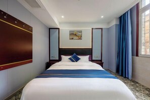 Quarto de hotel com uma cama grande, cabeceira com pintura, janela com cortinas azuis e luminária fixada na parede.