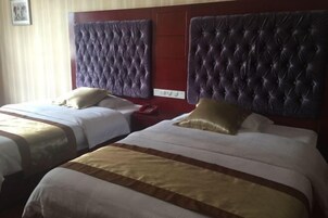 Quarto de hotel com duas camas, cada uma com cabeceira estofada, roupa de cama branca e uma faixa marrom.