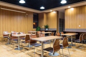 Uma área de refeições moderna com paredes de painel de madeira, mesas com estrutura de metal e cadeiras estofadas.