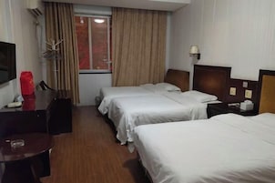 Quarto de hotel com duas camas de solteiro, uma mesa com cadeira, televisão e janela com cortinas.