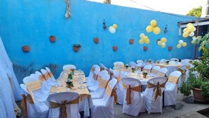 Uma área de refeições ao ar livre com mesas preparadas para um evento formal, decorada com detalhes em branco e dourado.