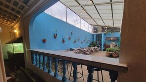 Zona de bar com paredes azuis, plantas em vasos e mesas ao ar livre.