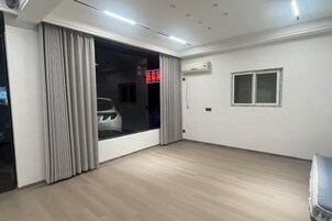 Um quarto com uma janela grande, uma porta, uma luminária no teto e um aparelho de ar condicionado.
