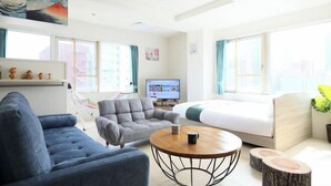Quarto de hotel moderno com sofá, poltrona, mesa de centro redonda e cama com cabeceira de madeira.