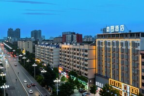 Um hotel com vários andares e uma placa grande, rua movimentada com carros e céu limpo.