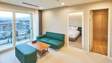 Quarto de hotel moderno com um sofá verde, uma mesa de centro de madeira e uma varanda com vista para a cidade.