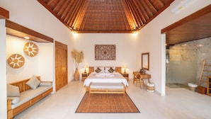 Quarto espaçoso com cama grande, teto de madeira e área de chuveiro visível através de uma porta de vidro.