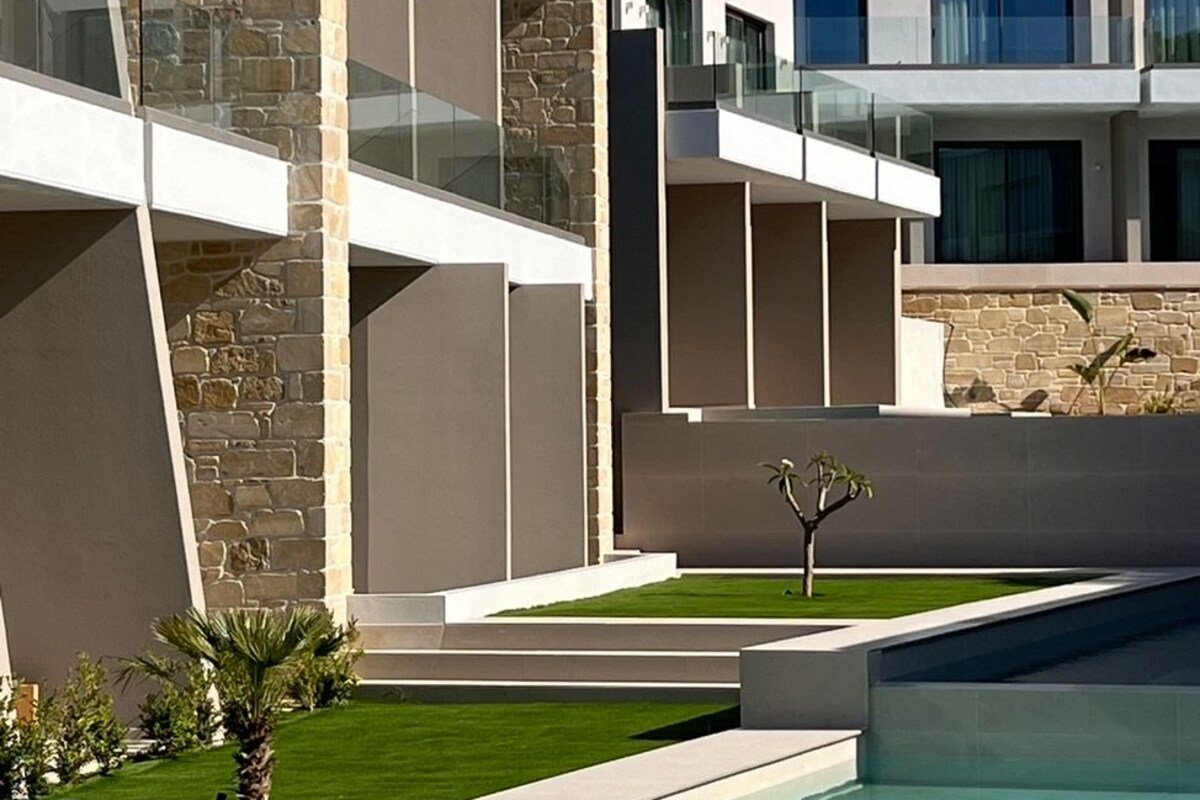 Um edifício moderno com piscina, fachada de pedra e várias varandas.