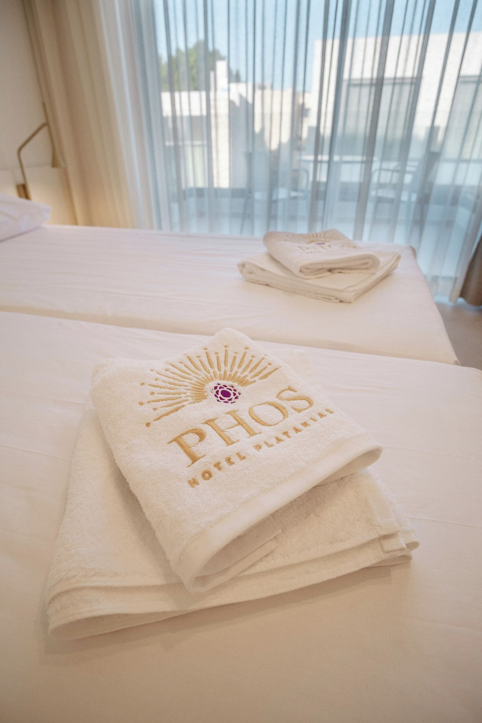 Quarto de hotel com duas camas, cada uma com uma toalha dobrada exibindo o nome do hotel.