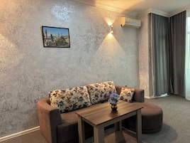 Uma sala de estar com um sofá, uma mesa de centro de madeira e um ar-condicionado fixado na parede.