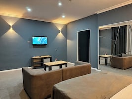Quarto moderno com televisão de tela plana na parede, sofá, mesa pequena e espelho.