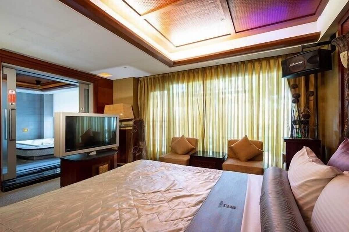 Quarto de hotel com cama, televisão, escrivaninha e janela com cortinas.