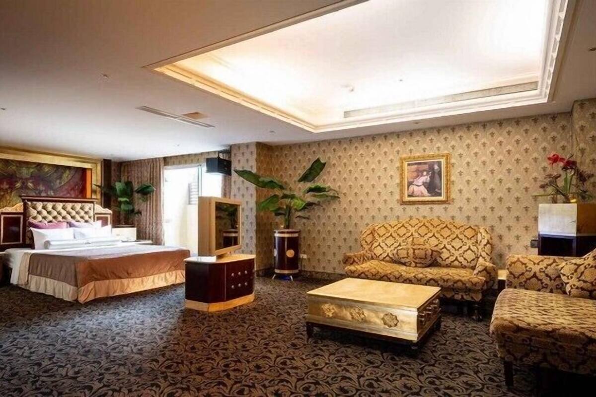 Quarto de hotel com cama, sofá, mesa de centro, televisão e uma janela grande.
