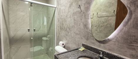 Casa de banho com chuveiro de vidro, sanita e lavatório com bancada de mármore.