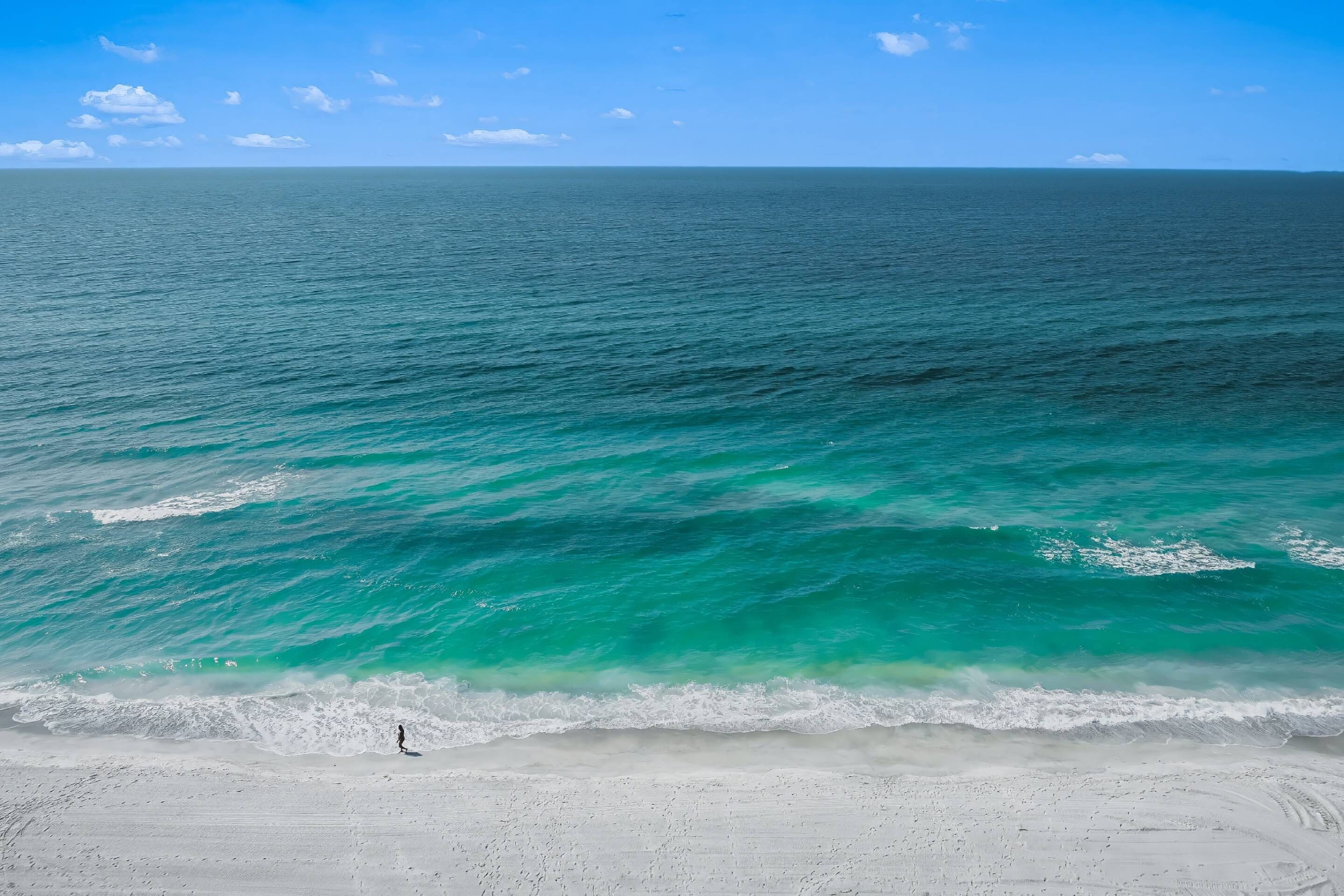 Uma praia com águas turquesa cristalinas e uma pessoa caminhando pela orla.