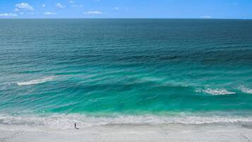 Uma praia com águas turquesa cristalinas e uma pessoa caminhando pela orla.