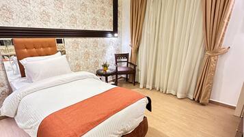 Quarto de hotel moderno com uma cama grande, uma mesinha de cabeceira com abajur e uma cadeira.