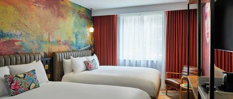 Quarto de hotel com duas camas, uma grande pintura abstrata na parede, uma escrivaninha com cadeira e uma janela ampla com cortinas.